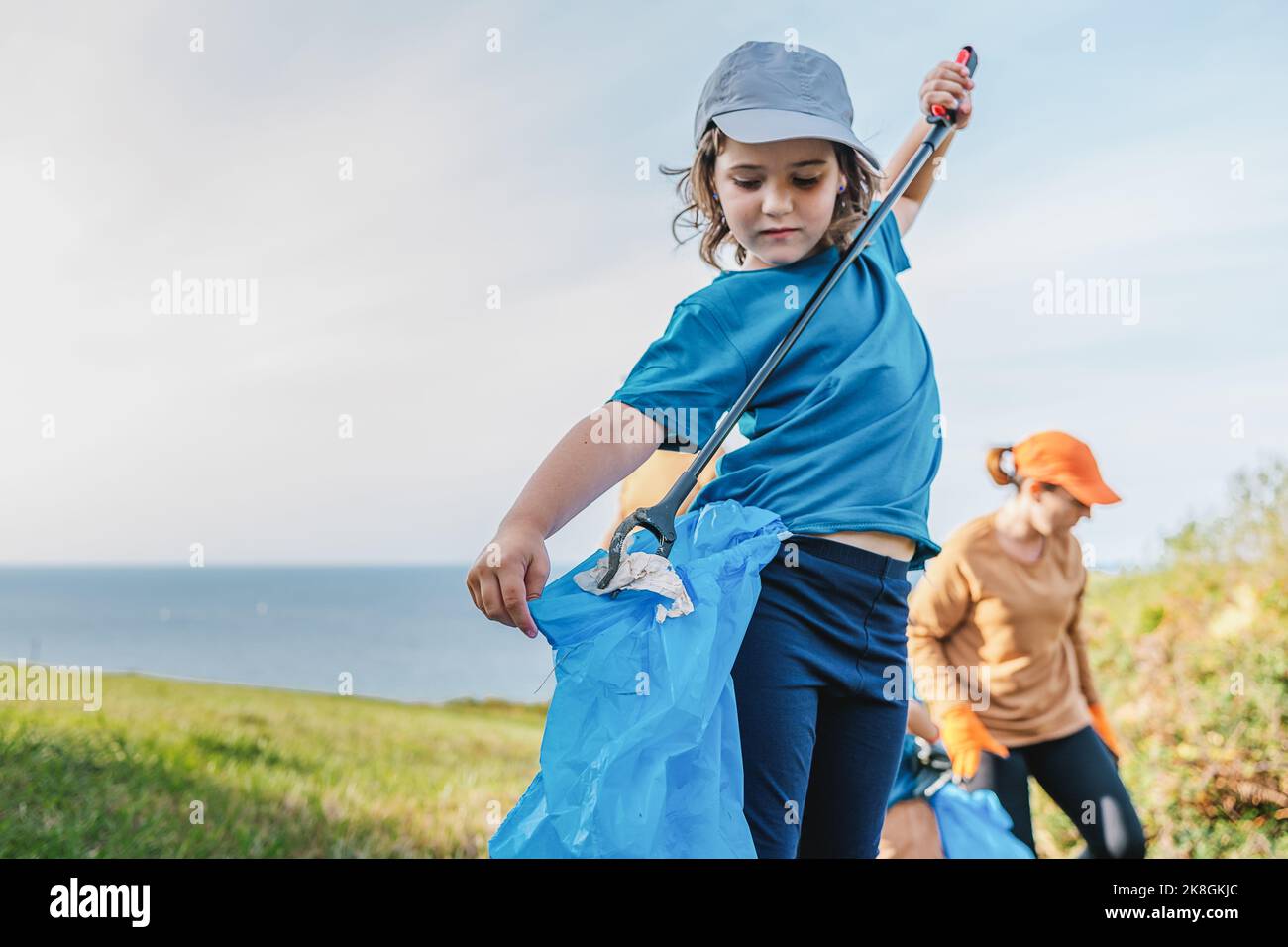 Adorable little volunteer in uniform collecting trash in plastic bag ...