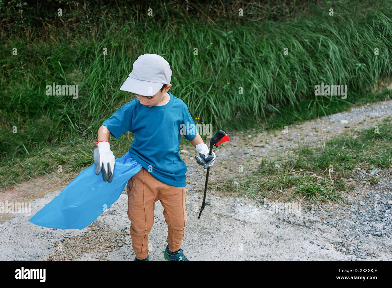 Adorable little volunteer in uniform collecting trash in plastic bag ...