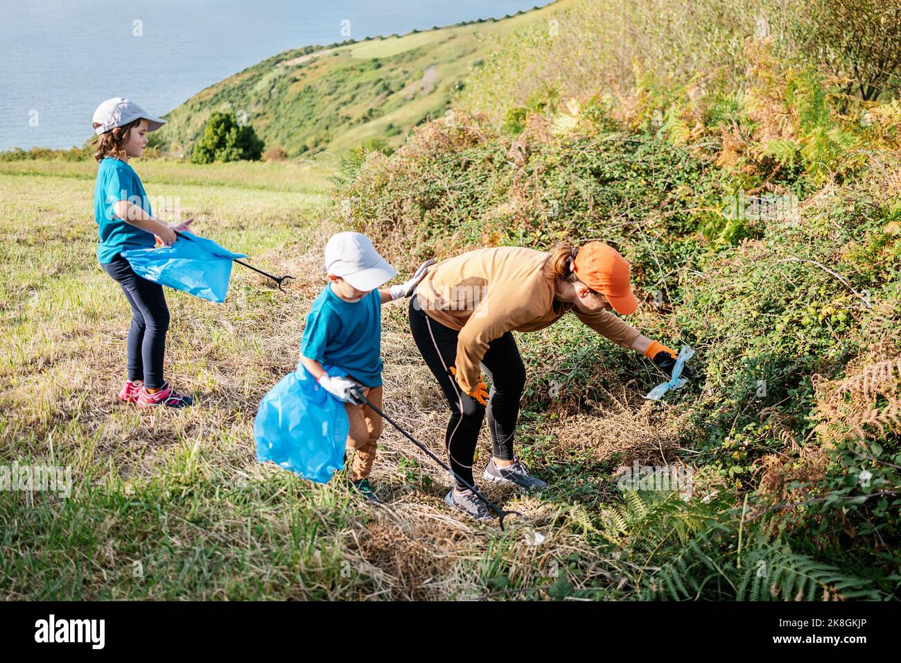 Cleanup volunteers picking up trash in garbage bags with sticks on ...