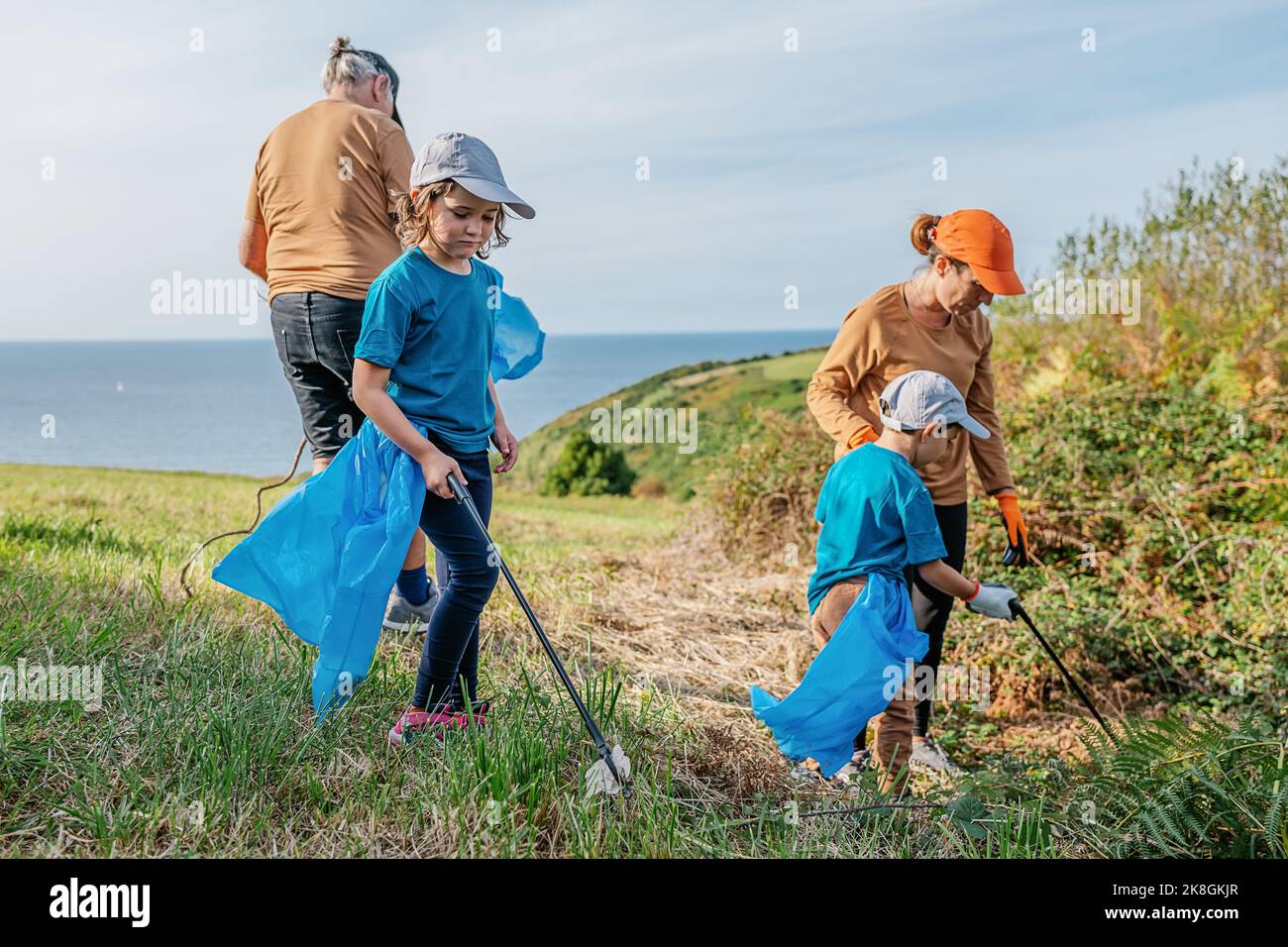 Cleanup volunteers picking up trash in garbage bags with sticks on ...