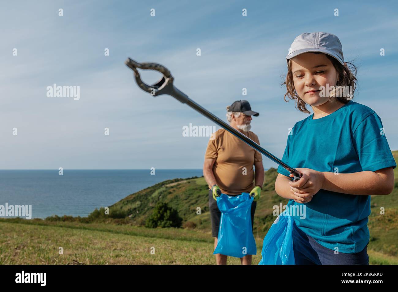 Preteen kid in blue t shirt and cap with trash tongs standing near aged ...