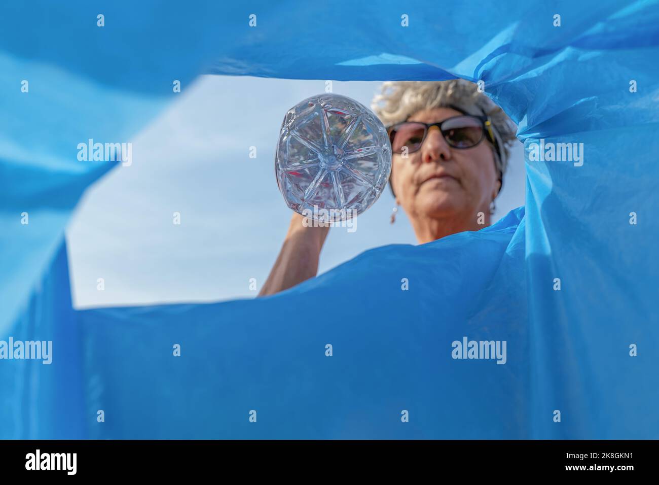 From below of aged female volunteer throwing trash into bin bag during ...