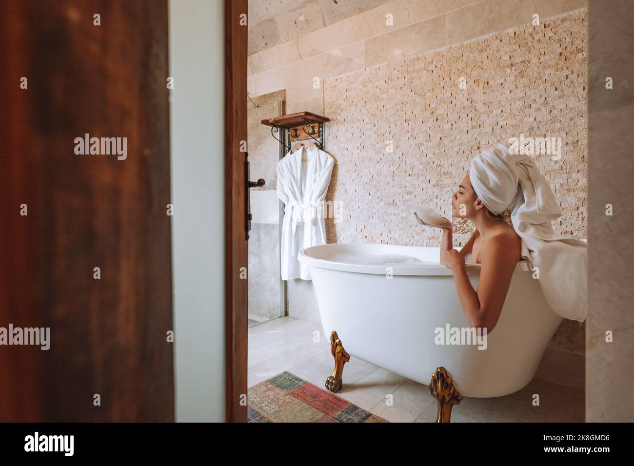 Side view of young female with white towel on head blowing on lather ...