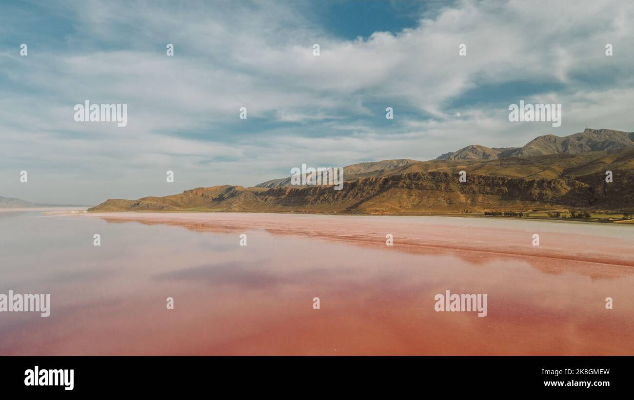 Pink water of Maharloo lake located near mountain ridge against cloudy ...