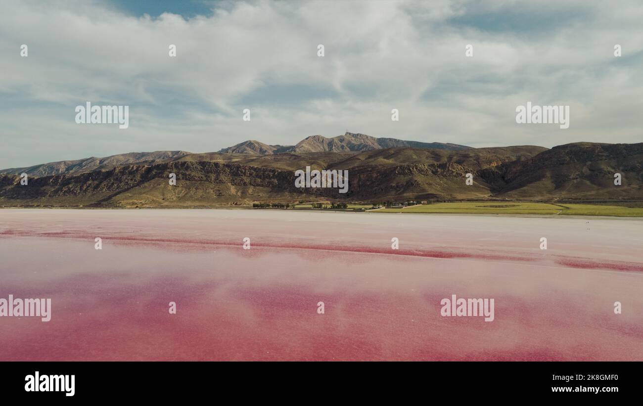 Pink water of Maharloo lake located near mountain ridge against cloudy ...