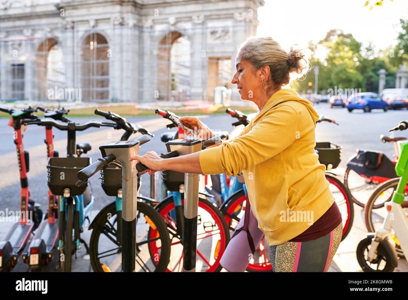 Side view of elderly female athlete with rolled up mat using smartphone ...