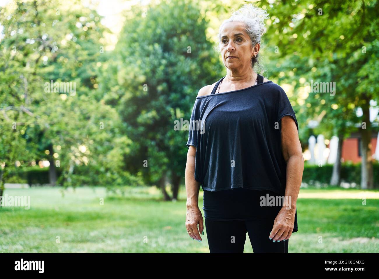 Calm unemotional elderly woman in black sportswear with bun hairstyle ...
