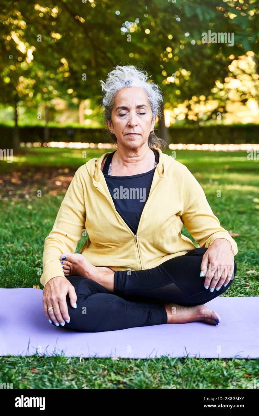 Barefoot aged woman in activewear closing eyes and meditating while ...