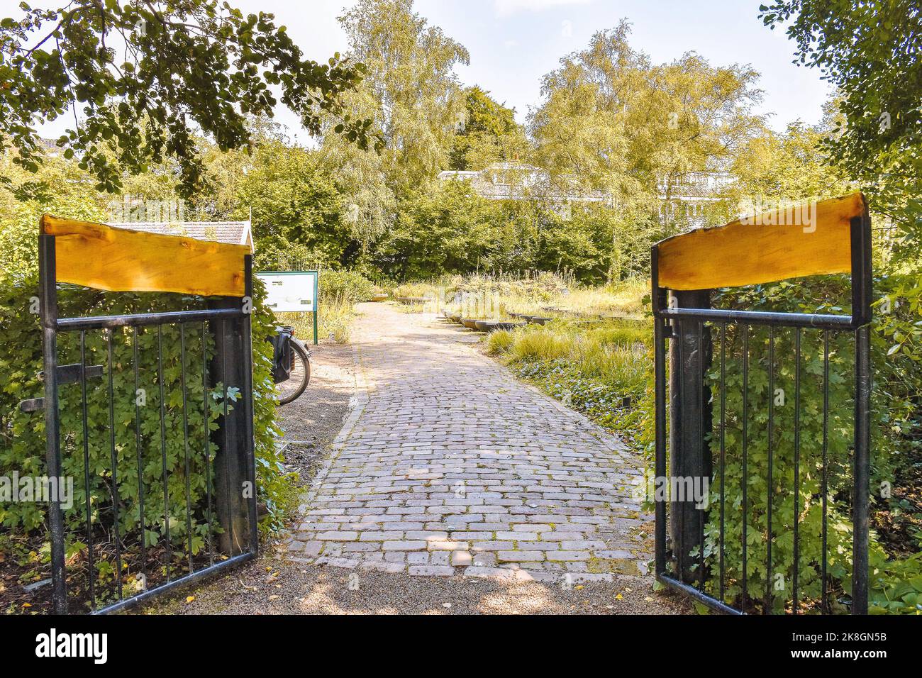 Open iron gate to a forest with cobblestone path Stock Photo - Alamy