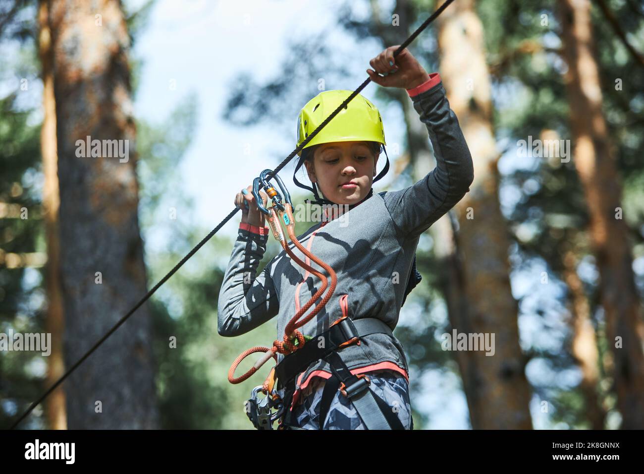 From below girl in activewear and helmet with safety ropes grasping ...