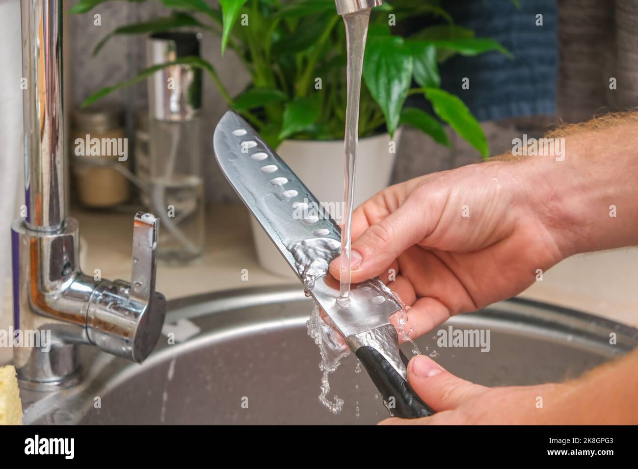 A man washes a sharp steel dirty kitchen knife with a sponge with ...