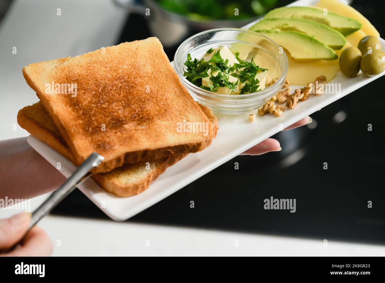 Woman's hand puts freshly baked toast on a plate. Sliced avocado ...