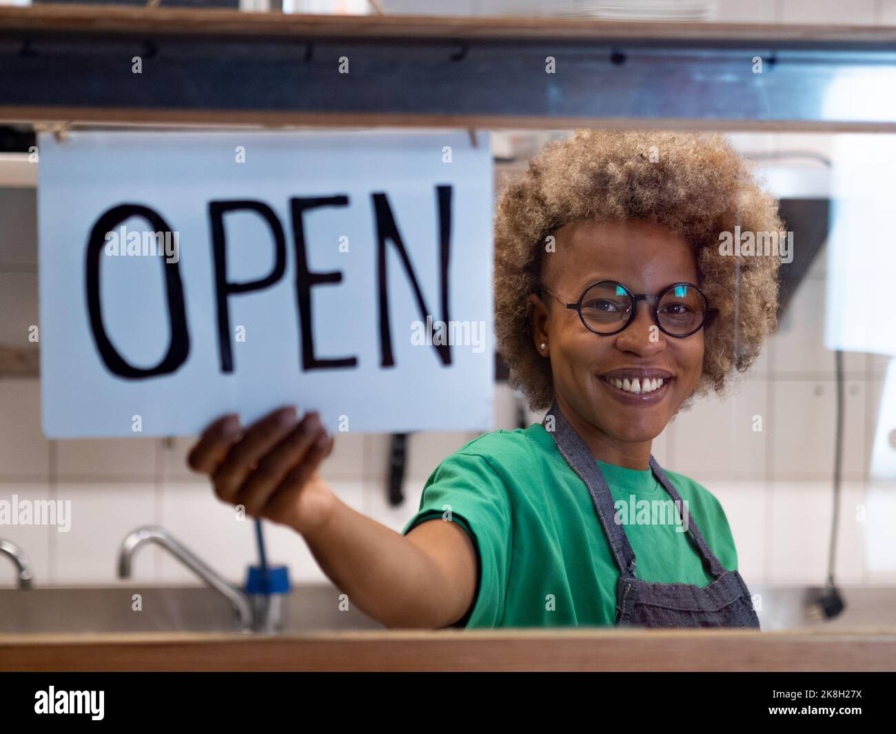 Happy African American woman looking at camera and Hanging Open Sign by ...