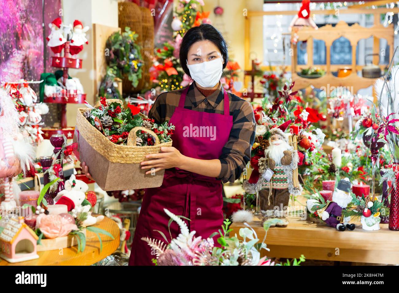 Flower shop employee wearing protective mask with basket of christmas ...