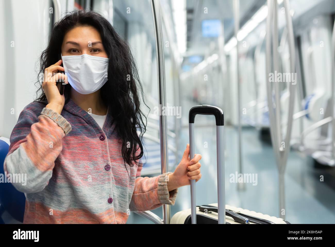 Woman traveler in a protective mask talking on a mobile phone in subway ...