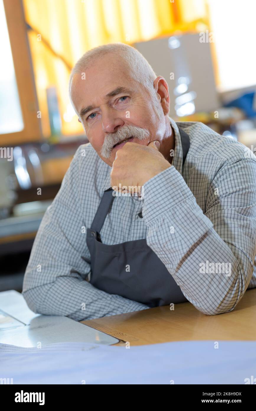elderly worker on apron sitting posing Stock Photo - Alamy
