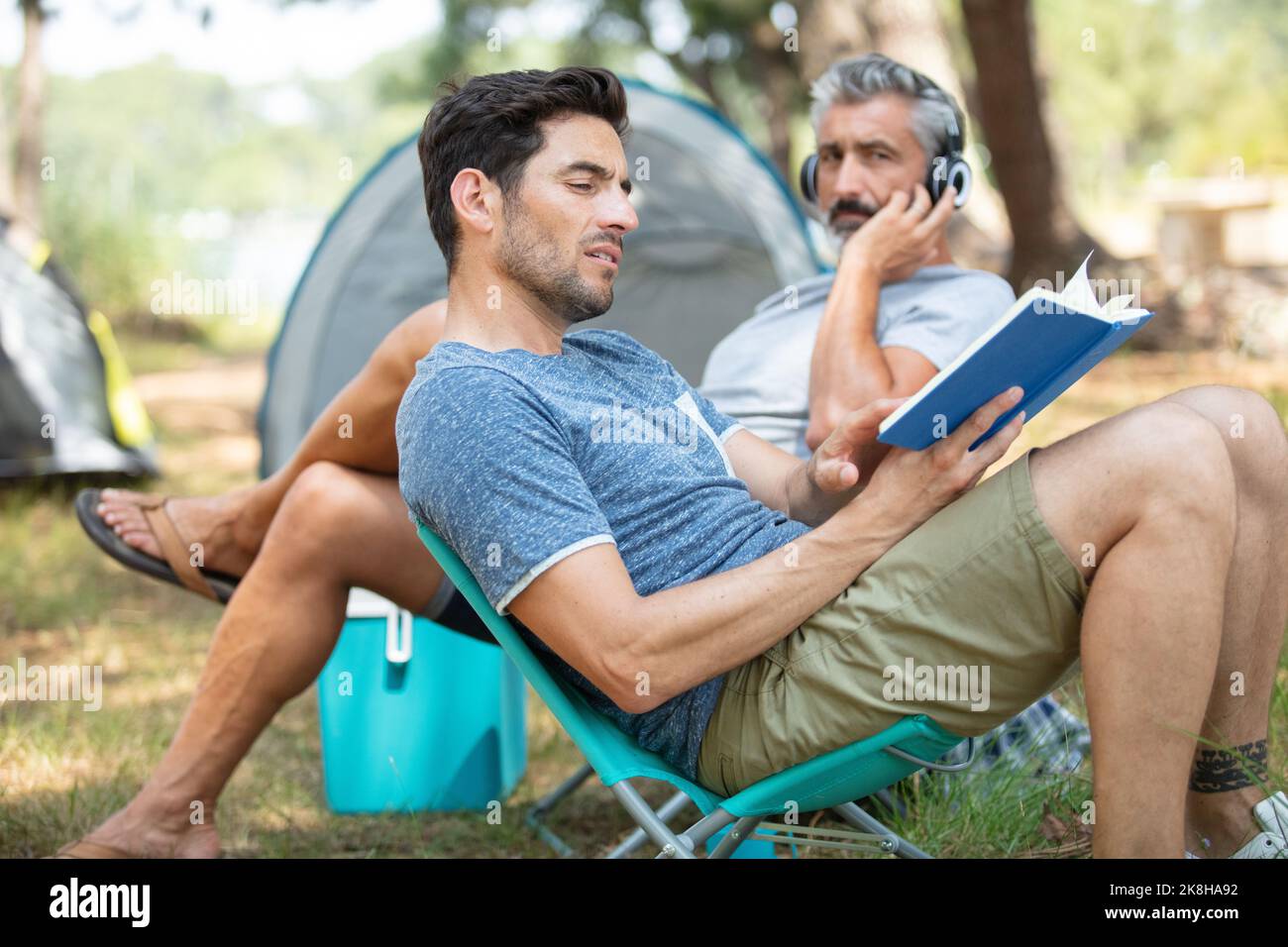men on camping holiday reading a book Stock Photo - Alamy