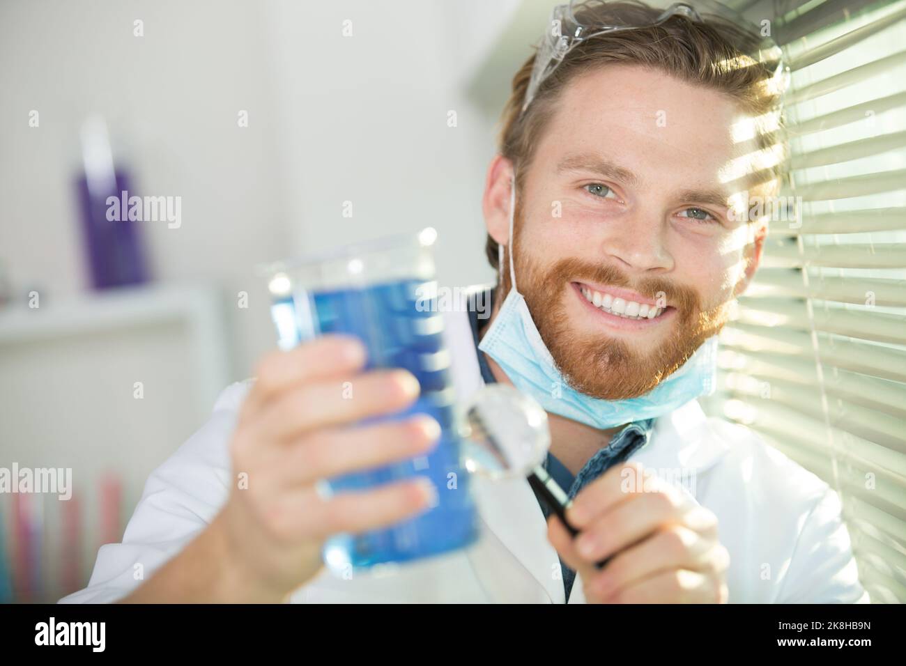 young chemist looking at beaker through a magnifying glass Stock Photo ...