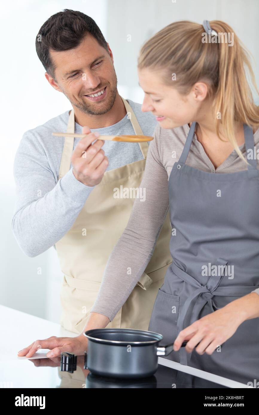 man preparing dinner and making her wife taste the food Stock Photo - Alamy