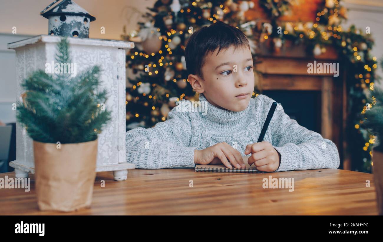 Portrait of thoughtful little boy writing letter to Santa Claus before ...