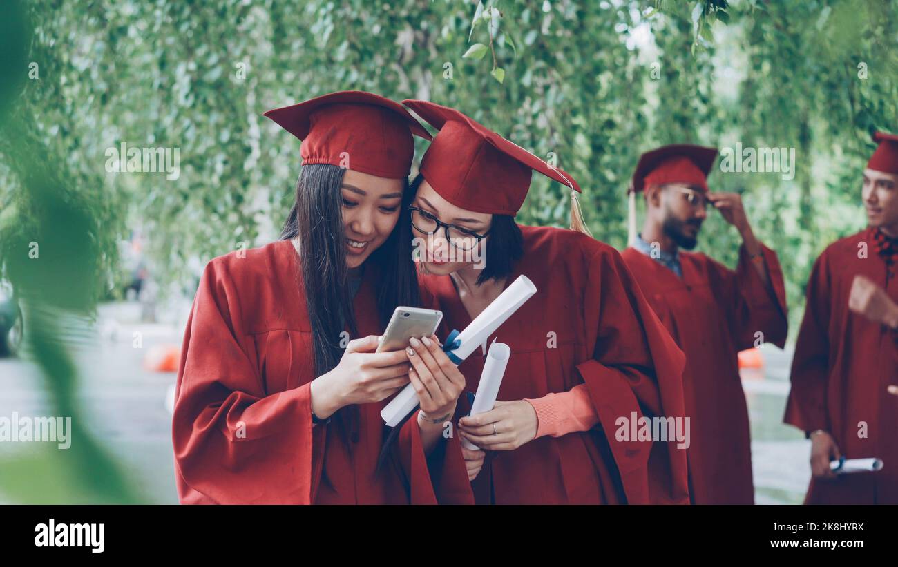 Female graduates are using smartphone looking at screen talking and ...