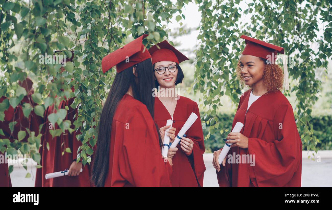 Three pretty girls graduates are talking and holding diplomas on ...