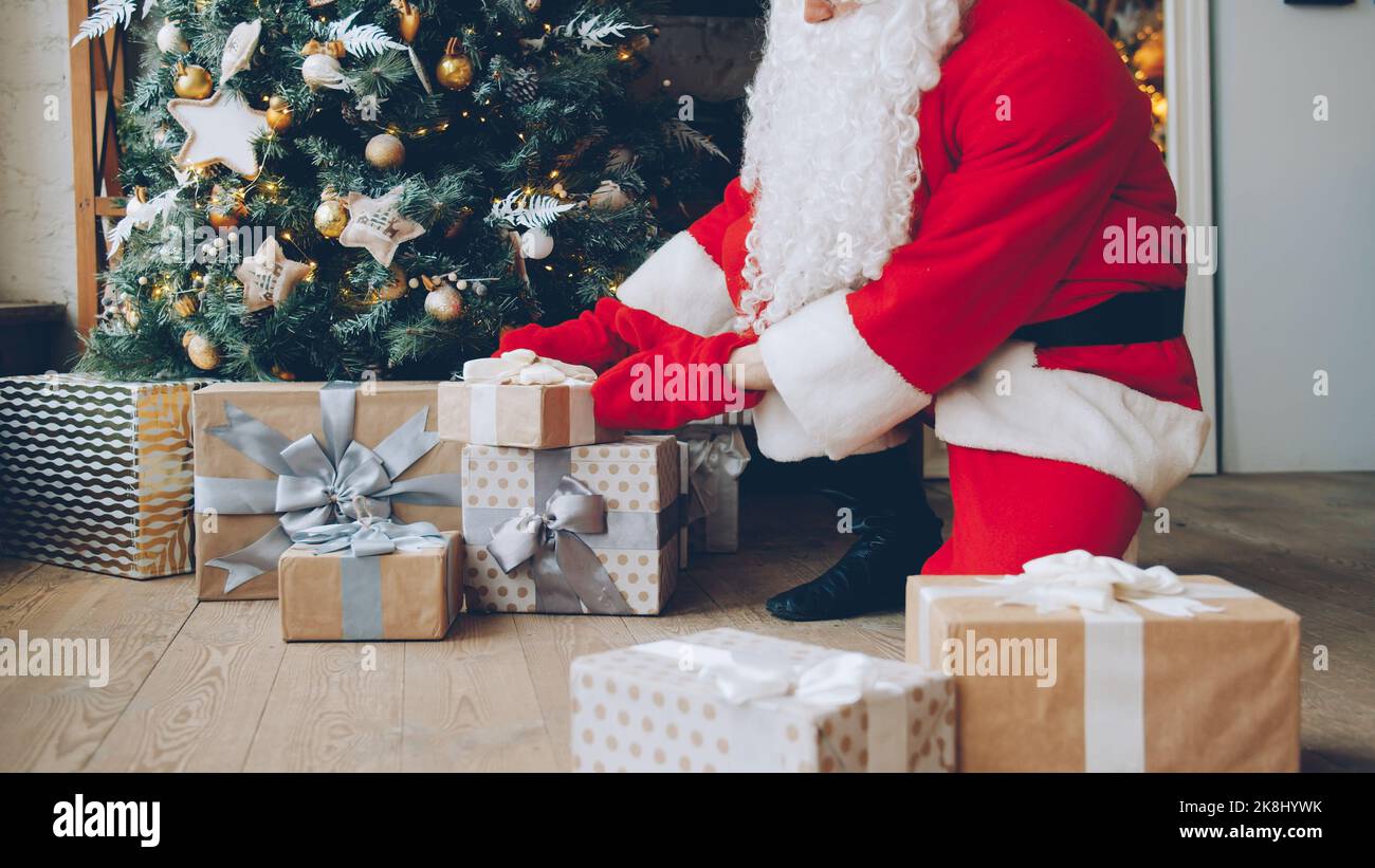 Santa Claus in traditional costume putting gift boxes under Christmas ...