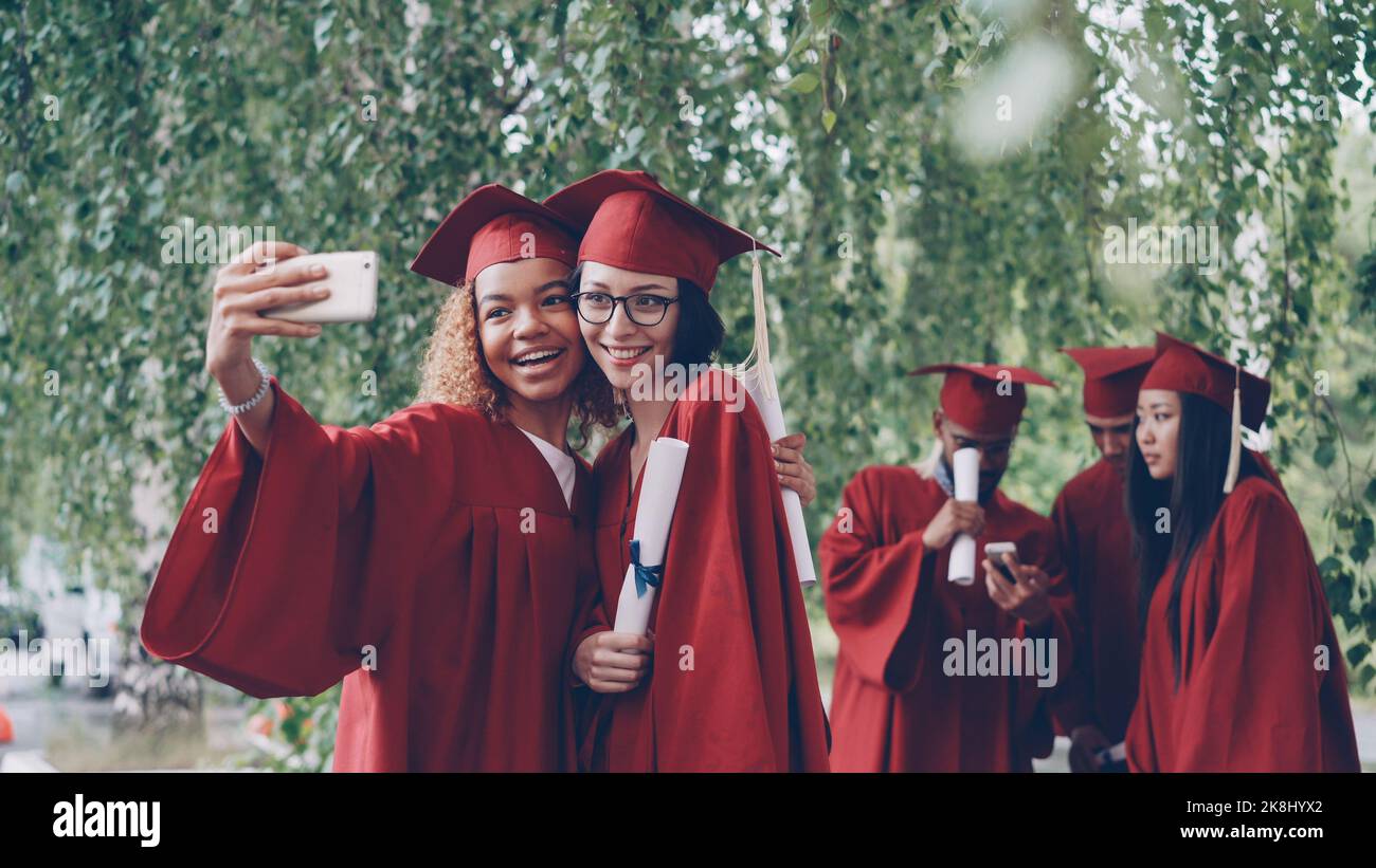 Pretty female graduates are taking selfie with diploma scroll using ... Pretty female graduates are taking selfie with diploma scroll using ...