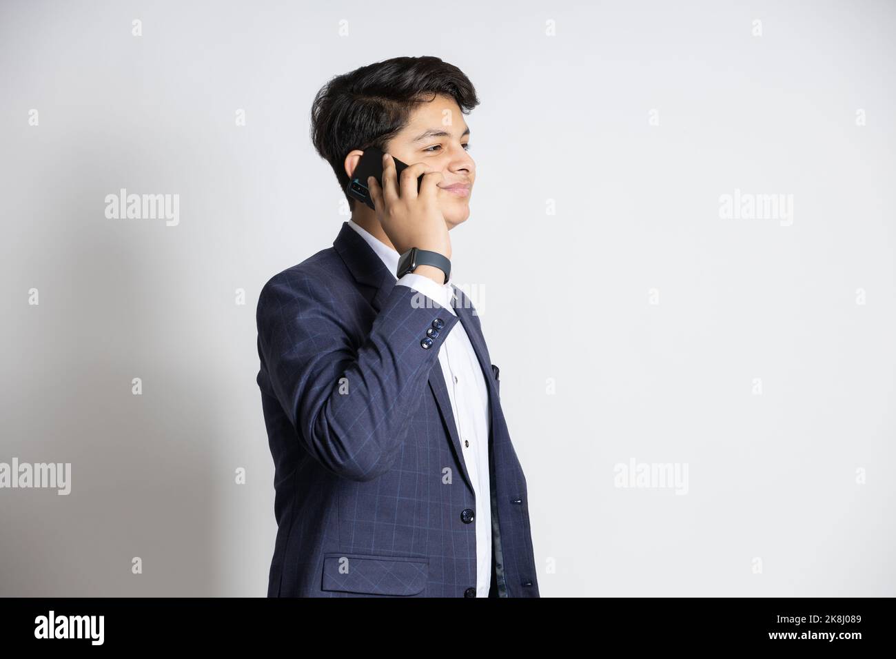Portrait of a young indian teenager boy wearing suit talking on phone ...