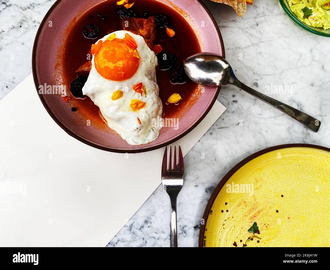 A fried egg dish with berries and flower petals. Fancy meal at a ...