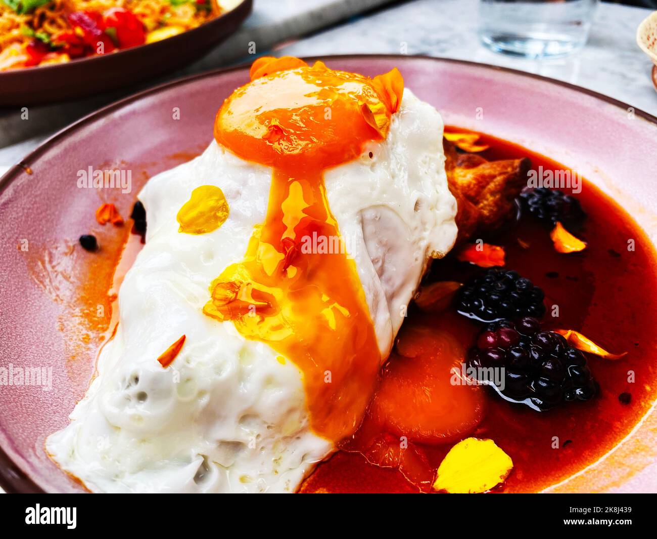 A fried egg dish with berries and flower petals. Fancy meal at a ...