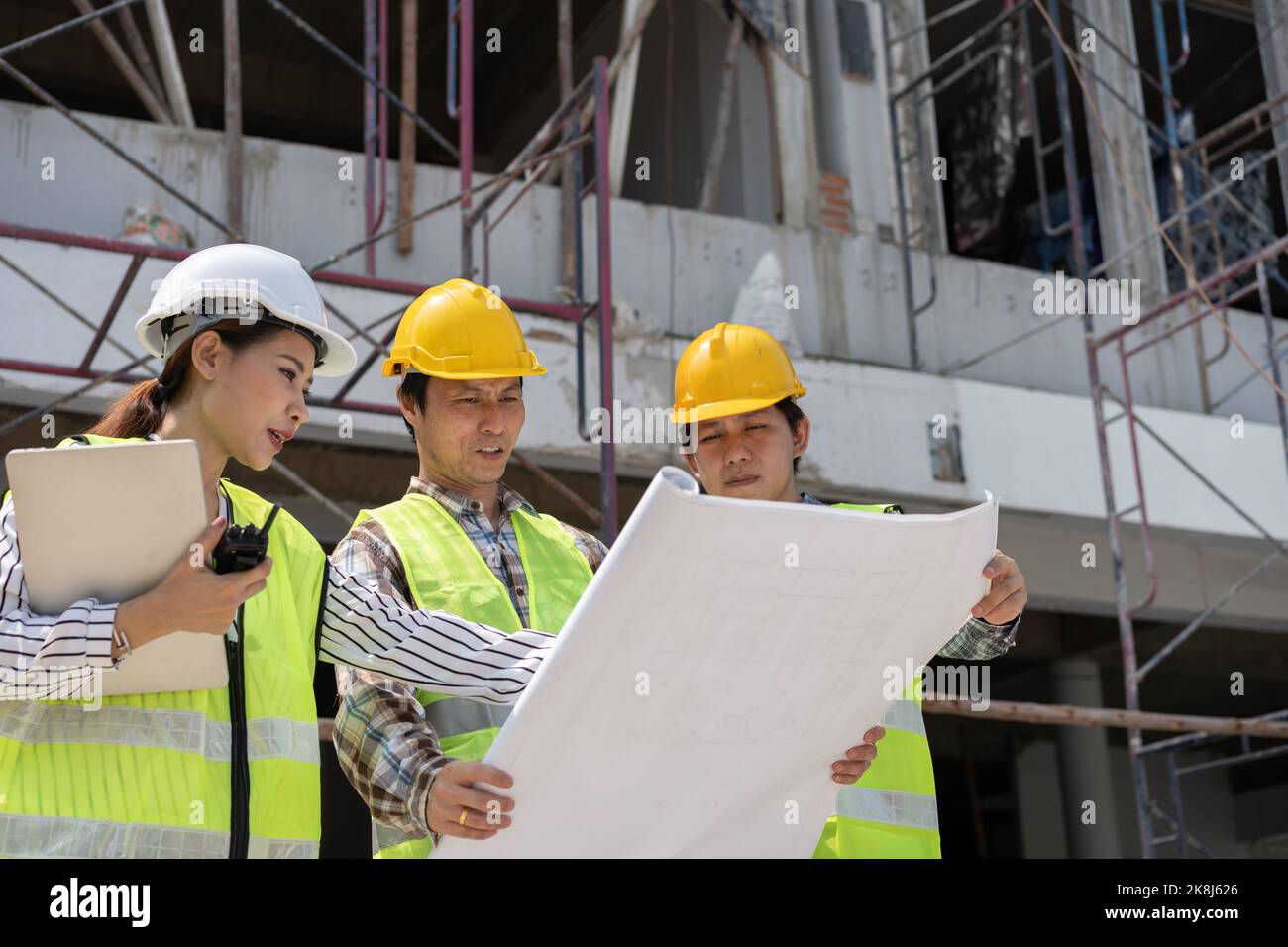 Asian engineer or Young Female Architect put on a helmet for safety and talk with a contractor ...