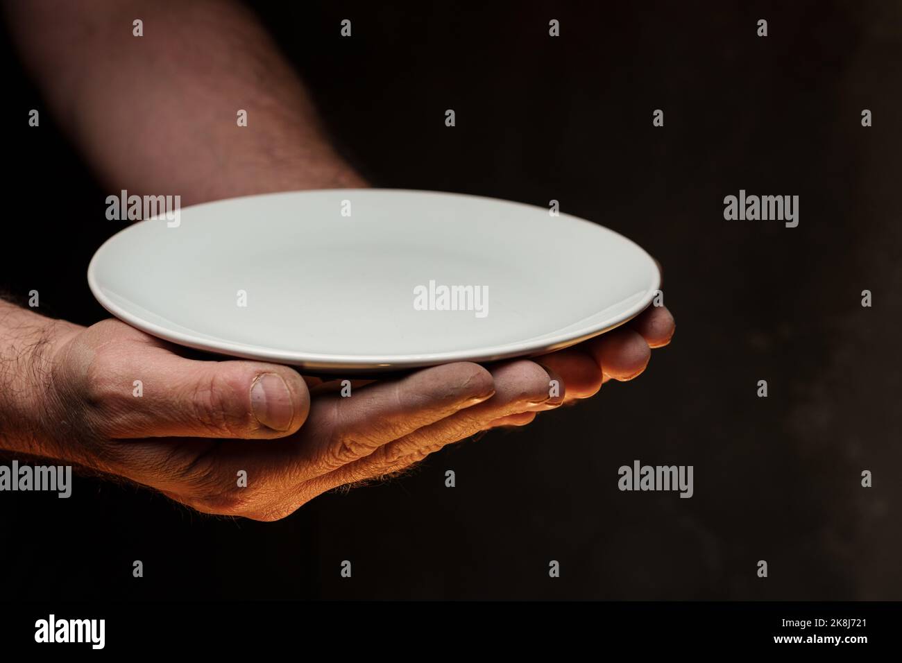 Male hands holding empty plate on dark background, lack of food, hunger ...