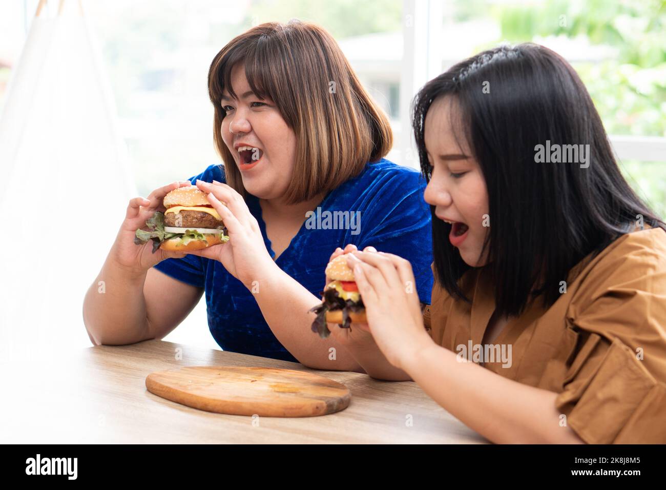 Hungry overweight woman holding hamburger on a wooden plate, During ...