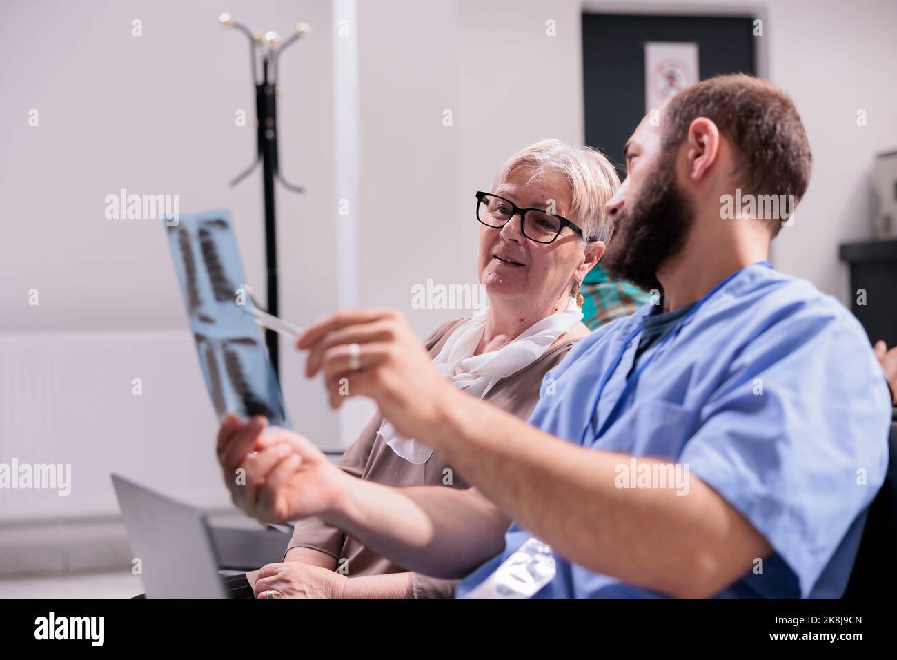 Male assistant hopsital staff showing x ray to elderly patient, in ...