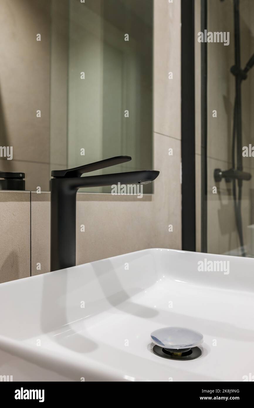Vertical close-up of modern black tap with white sink and mirror in a ...