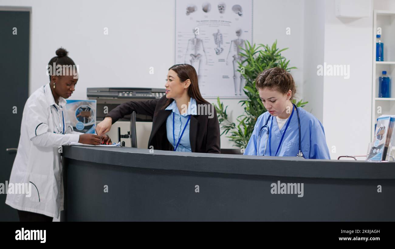 Medical assistant giving support to old patient at reception desk in ...