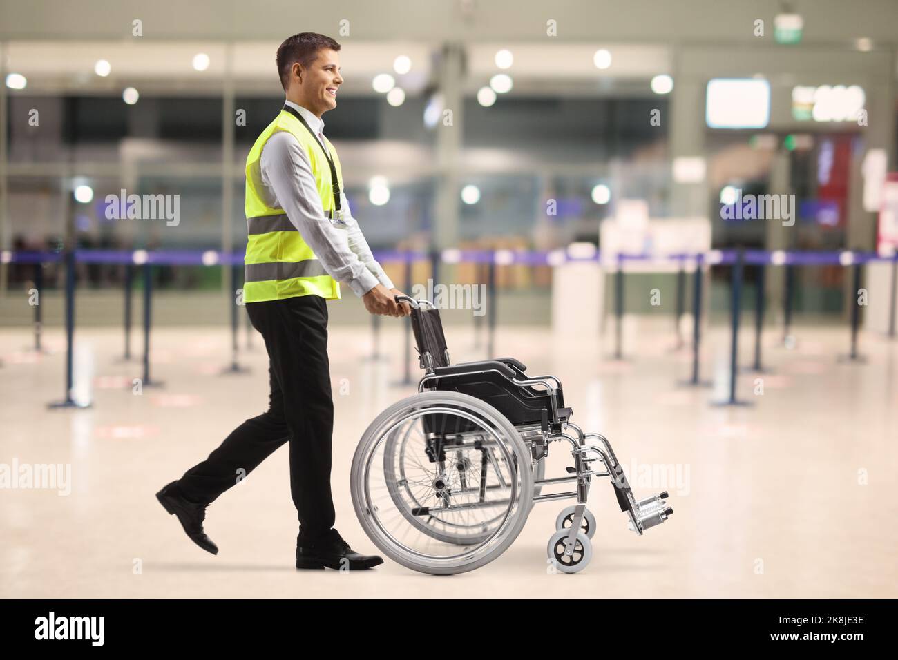 Airport employee pushing an empty wheelchair in a terminal building ...