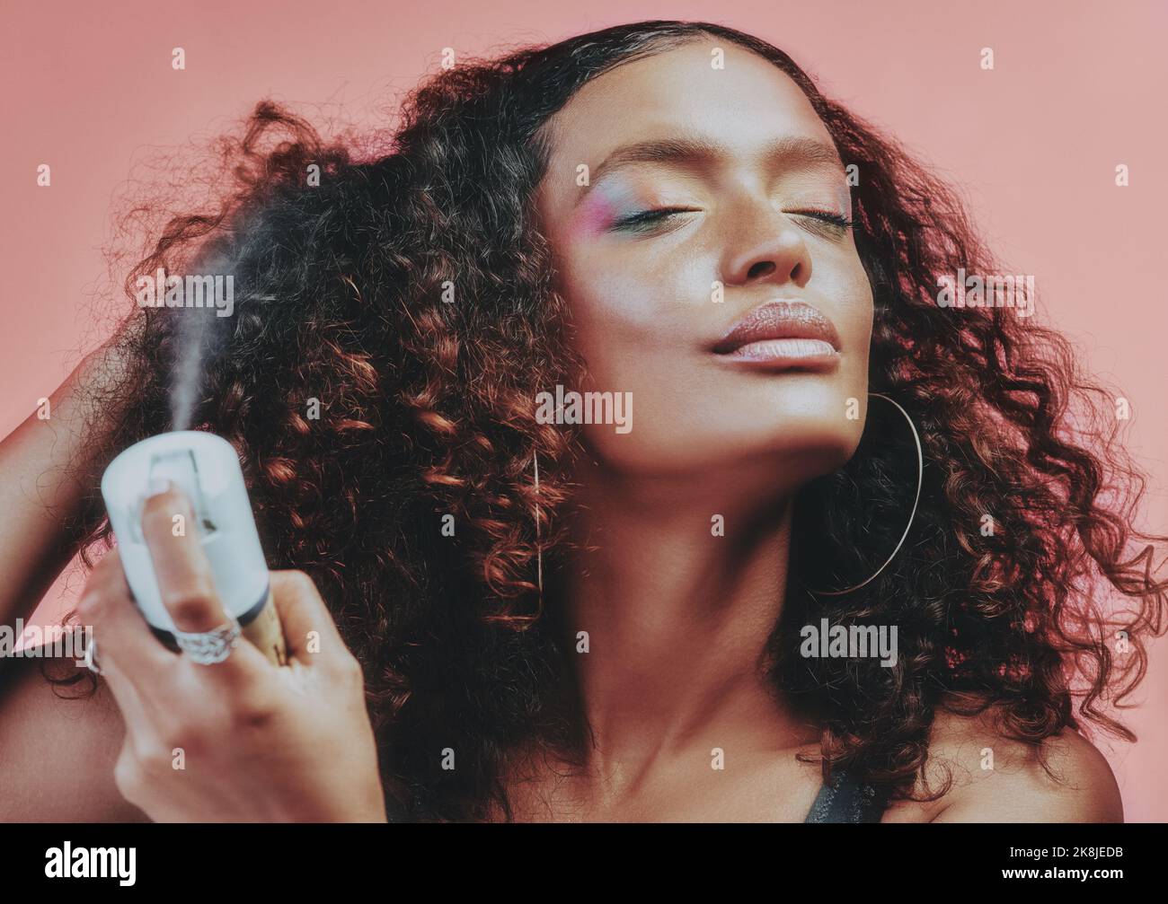 Put a hold on it. a young woman spraying hairspray on her curly hair ...