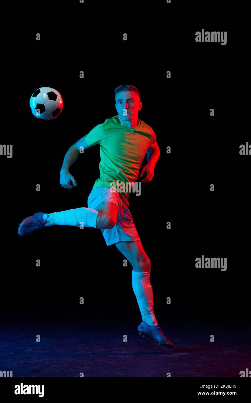 Dynamic shot of young active football player in action isolated on dark ...