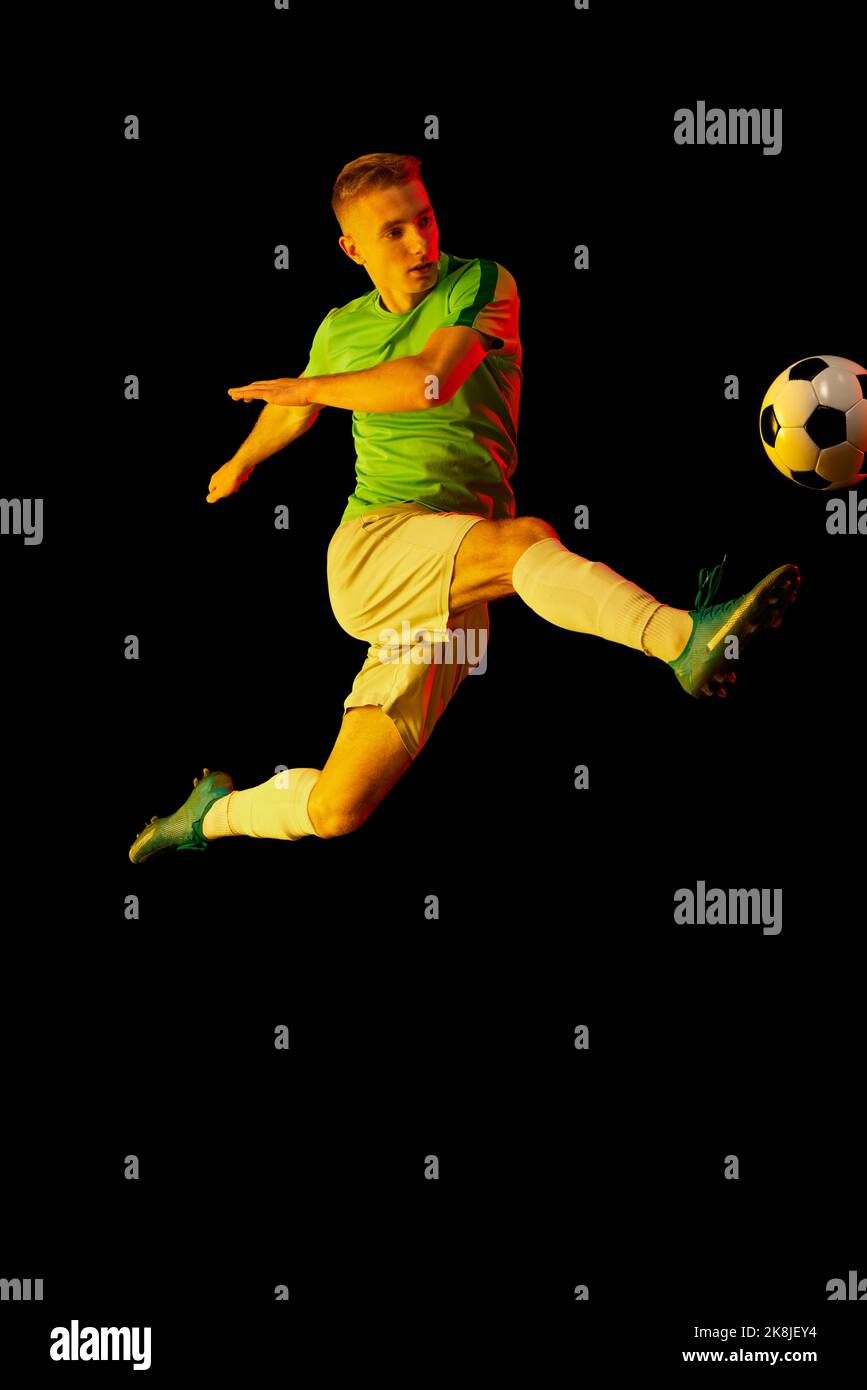 Dynamic shot of young active football player in action isolated on dark ...