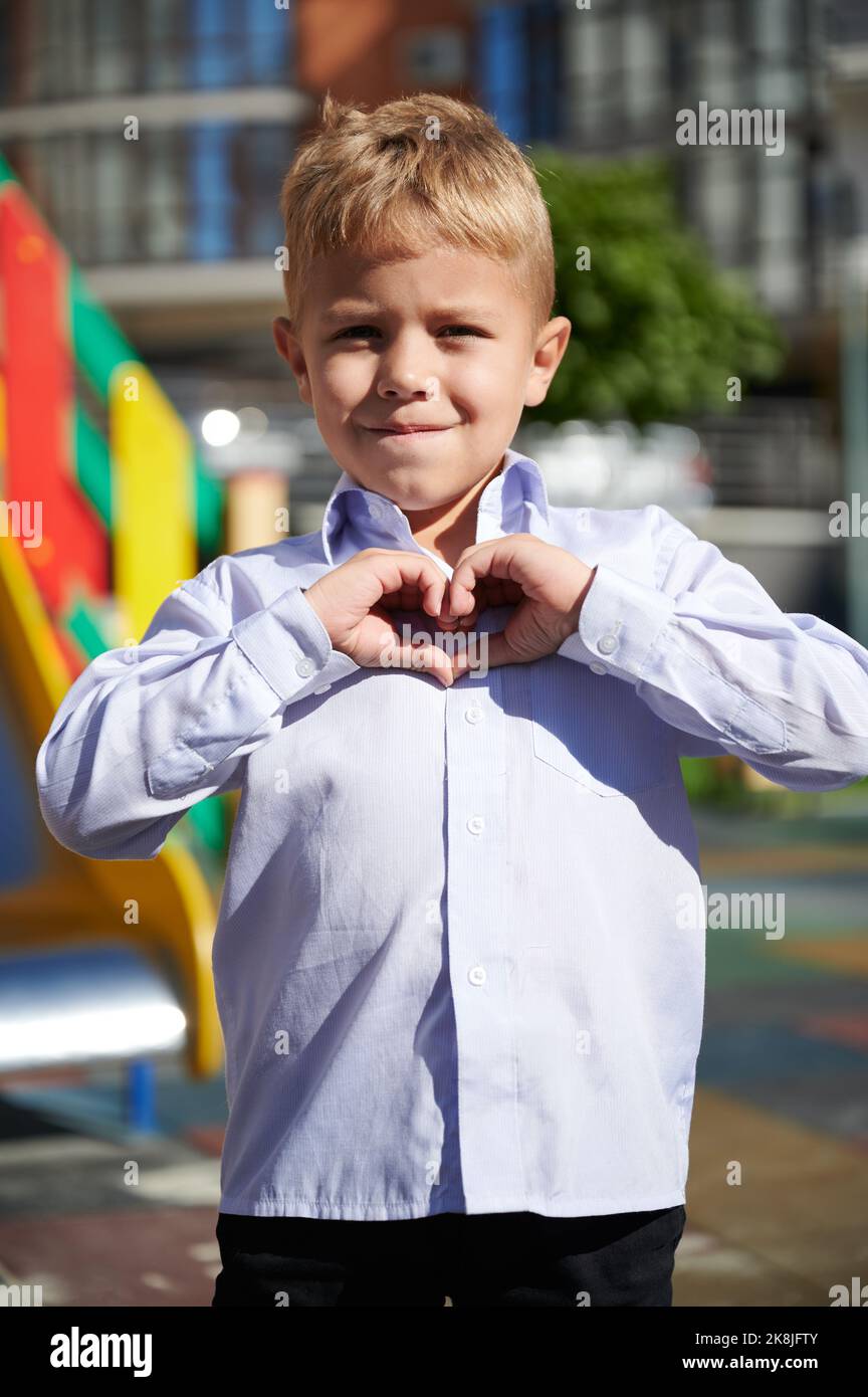 Portrait view of male kid shaping heart with hands and smiling at ...