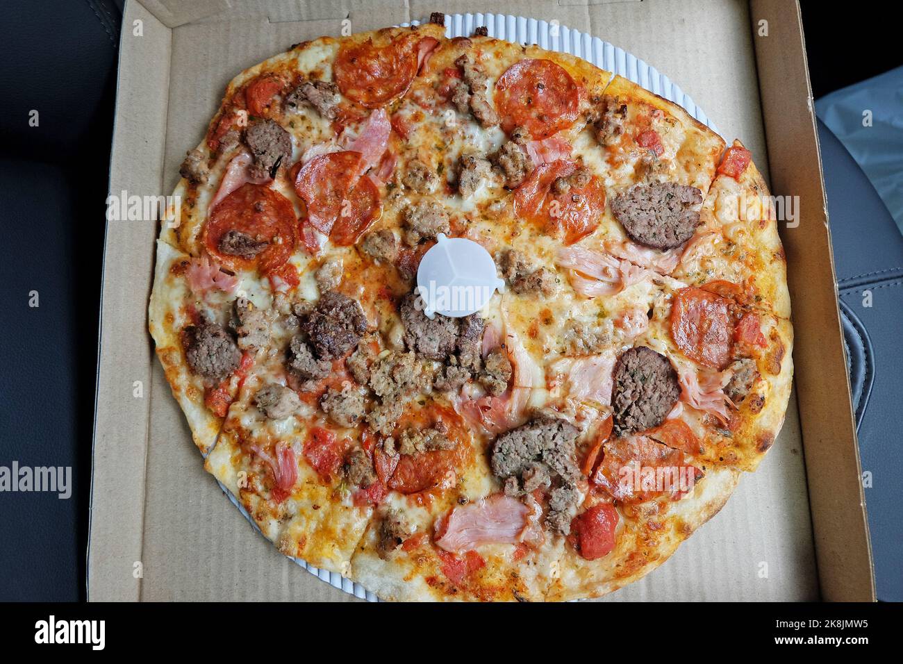 Close up box of Thin crust pizza topped with ham pepperoni and sausages ...