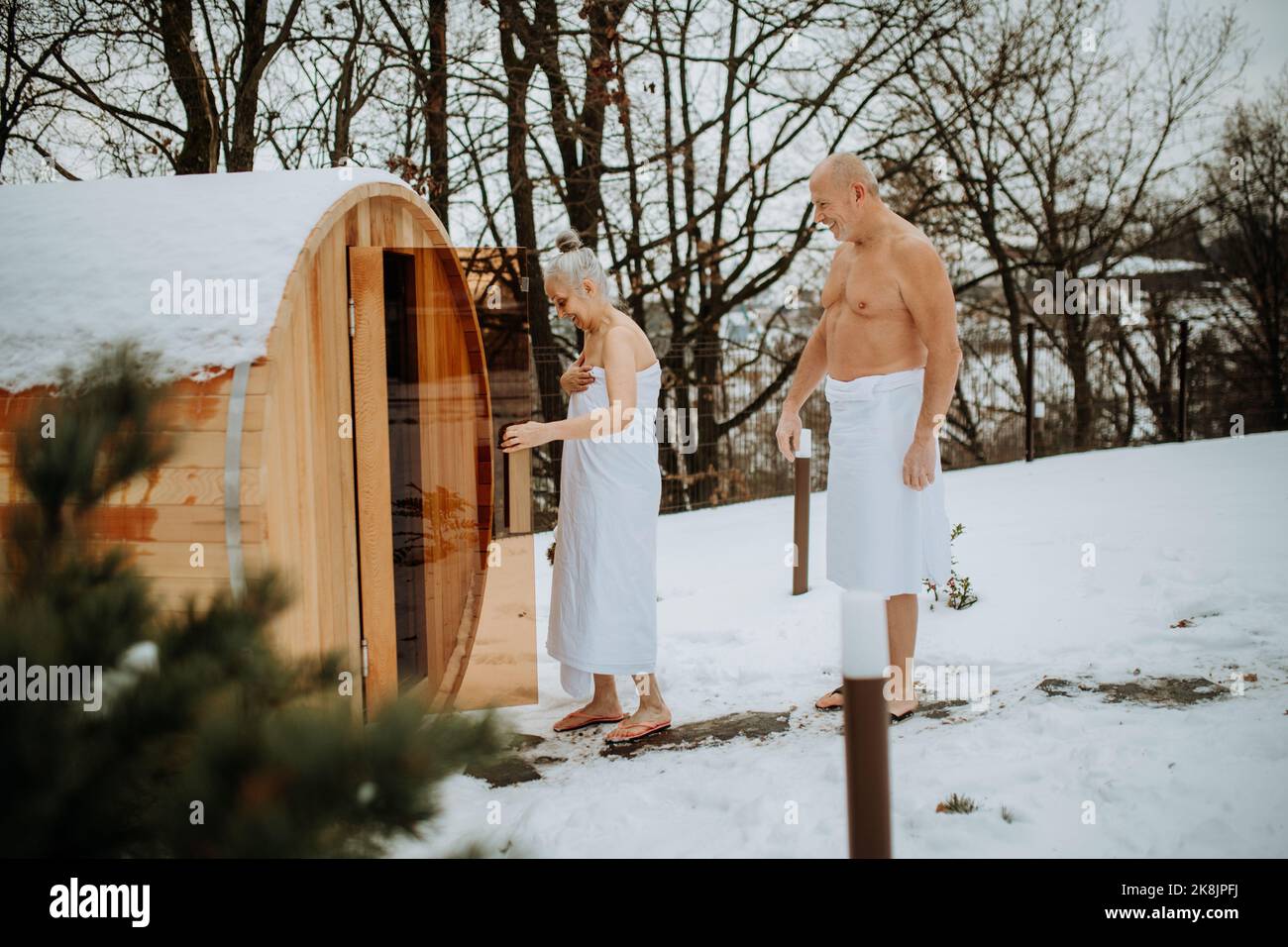 Senior Woman In Towel With Her Husband Entering To Outdoor Sauna During