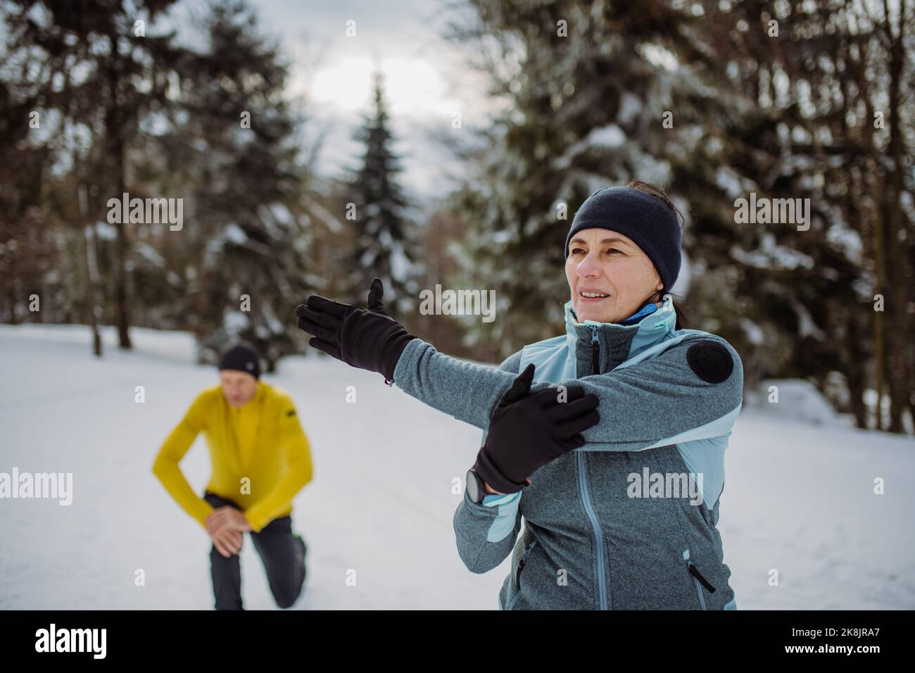 Senior couple warming-up and stretching in snowy forest before winter ...