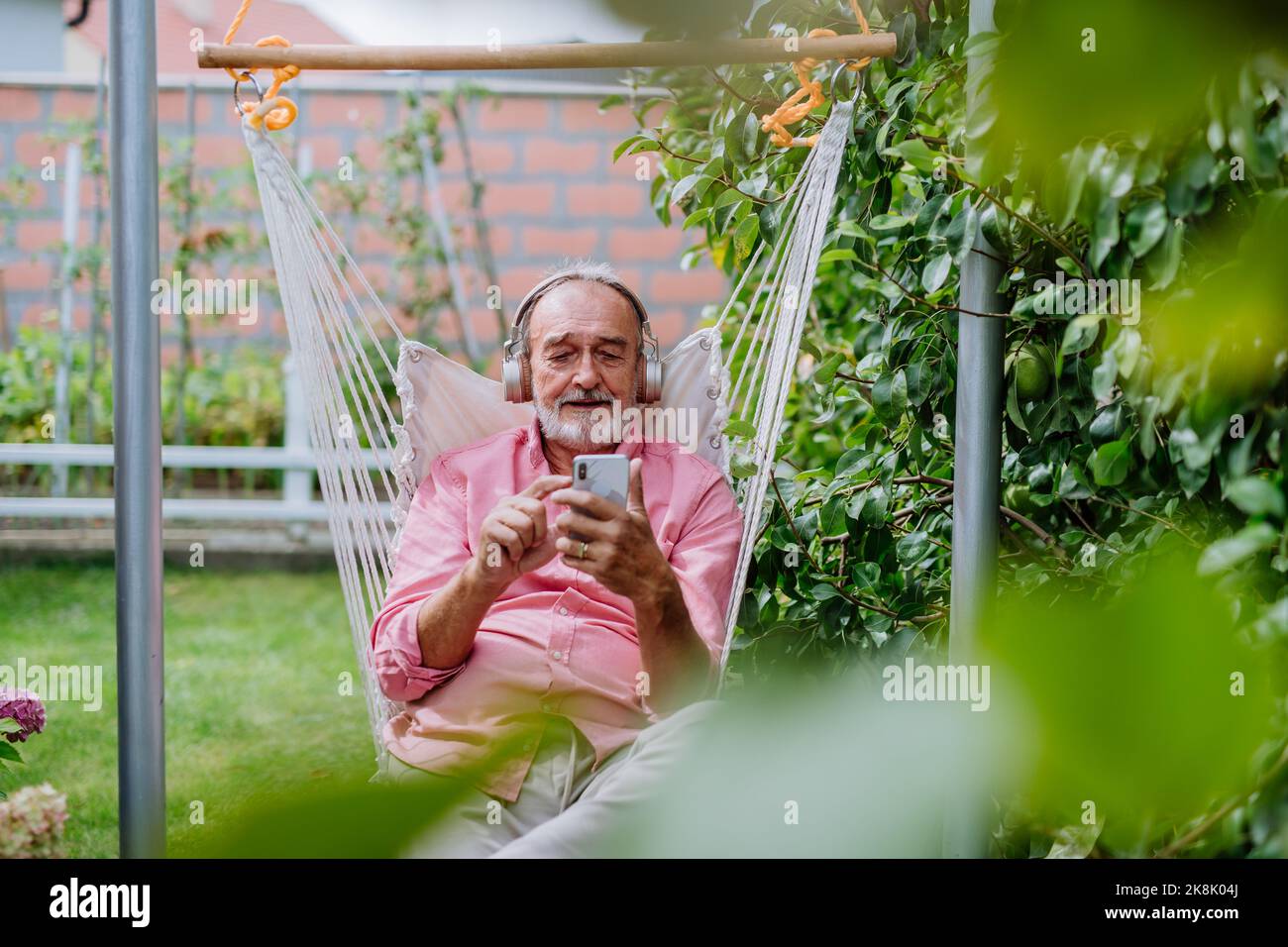 Happy senior man sitting in outdoor garden swing with headphones and ...
