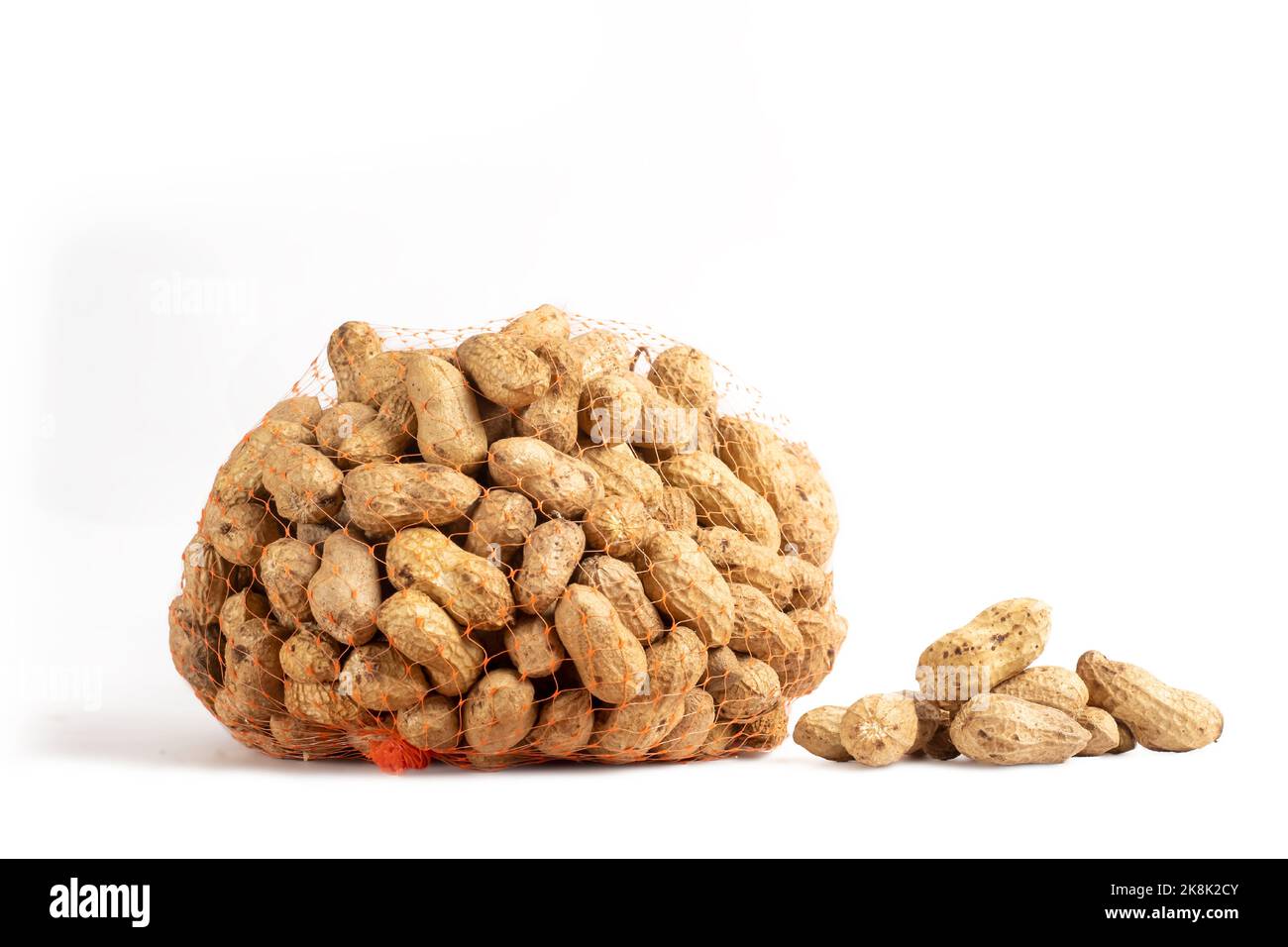 A mesh bag full of shelled peanuts next to scattered peanuts on a white ...