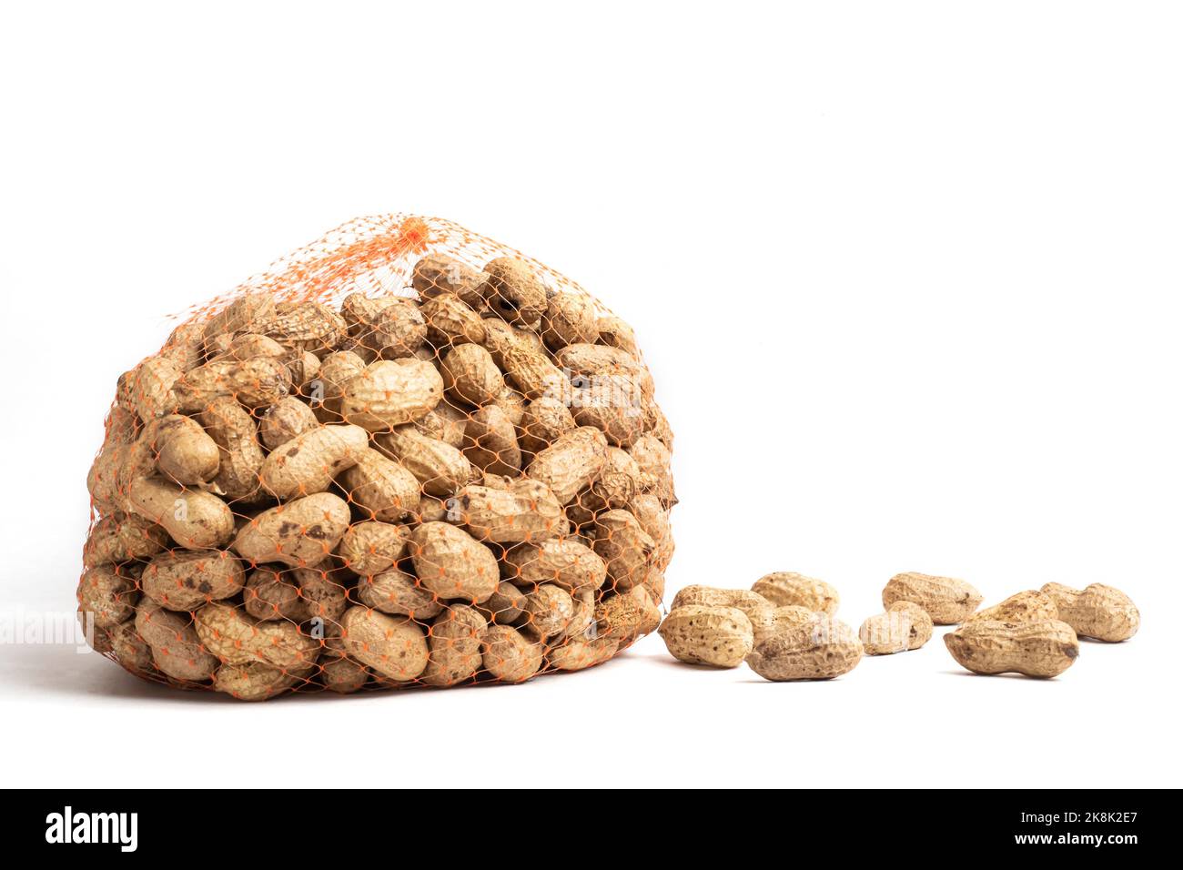 A mesh bag full of shelled peanuts next to scattered peanuts on a white ...