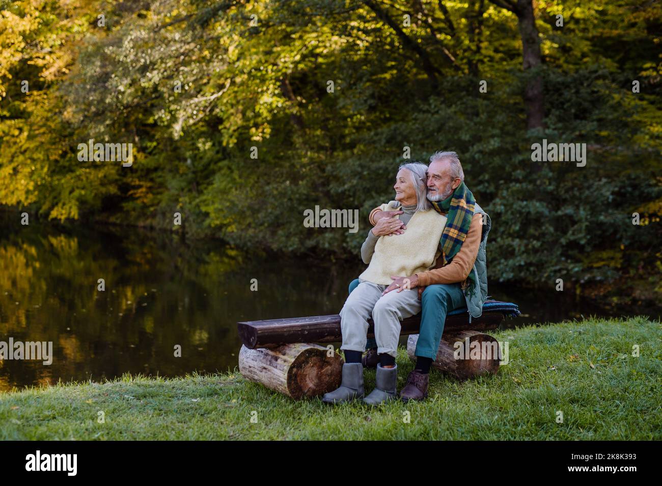 Senior couple in love sitting together on bench near lake, during ...