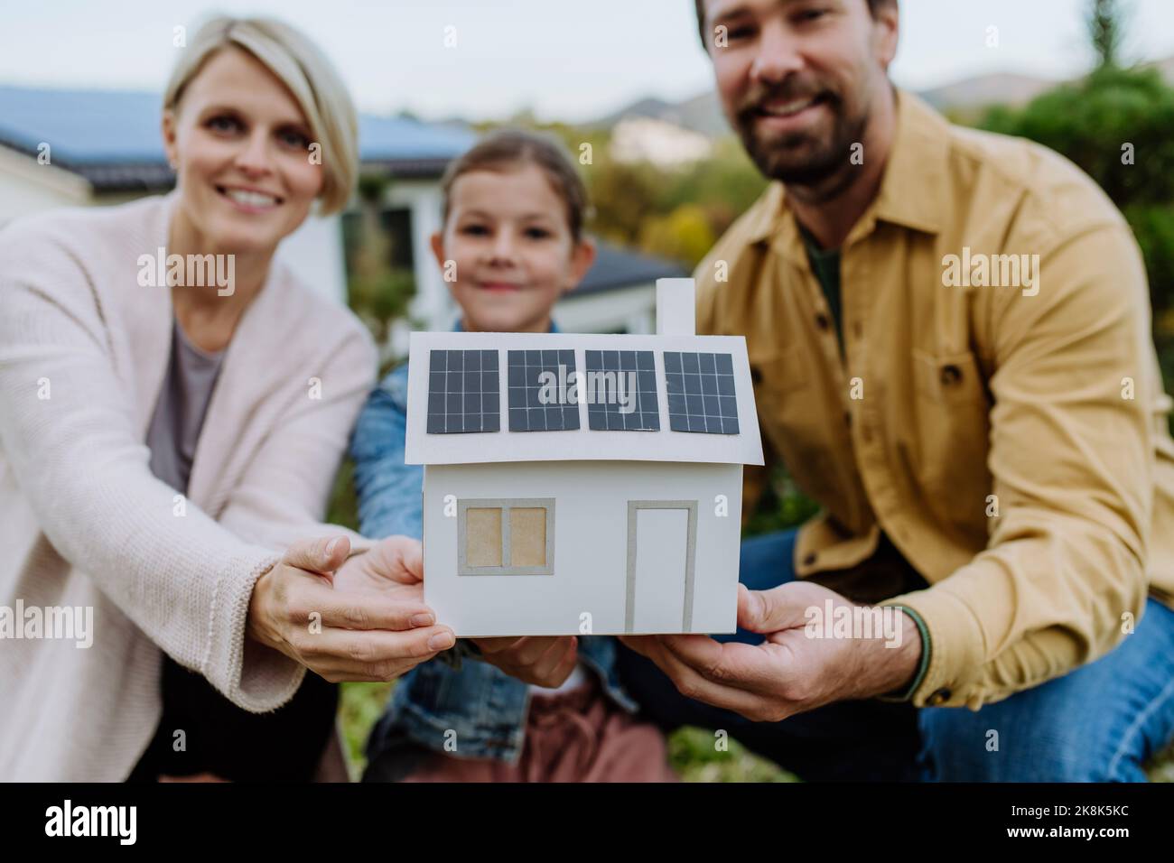 Happy family holding paper model of house with solar panels.Alternative ...